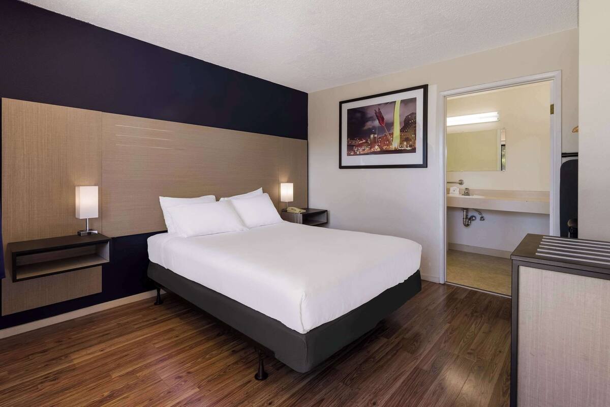 Quarto de hotel moderno com uma cama grande, mesas de cabeceira com luminárias, um espelho amplo e um quadro na parede.