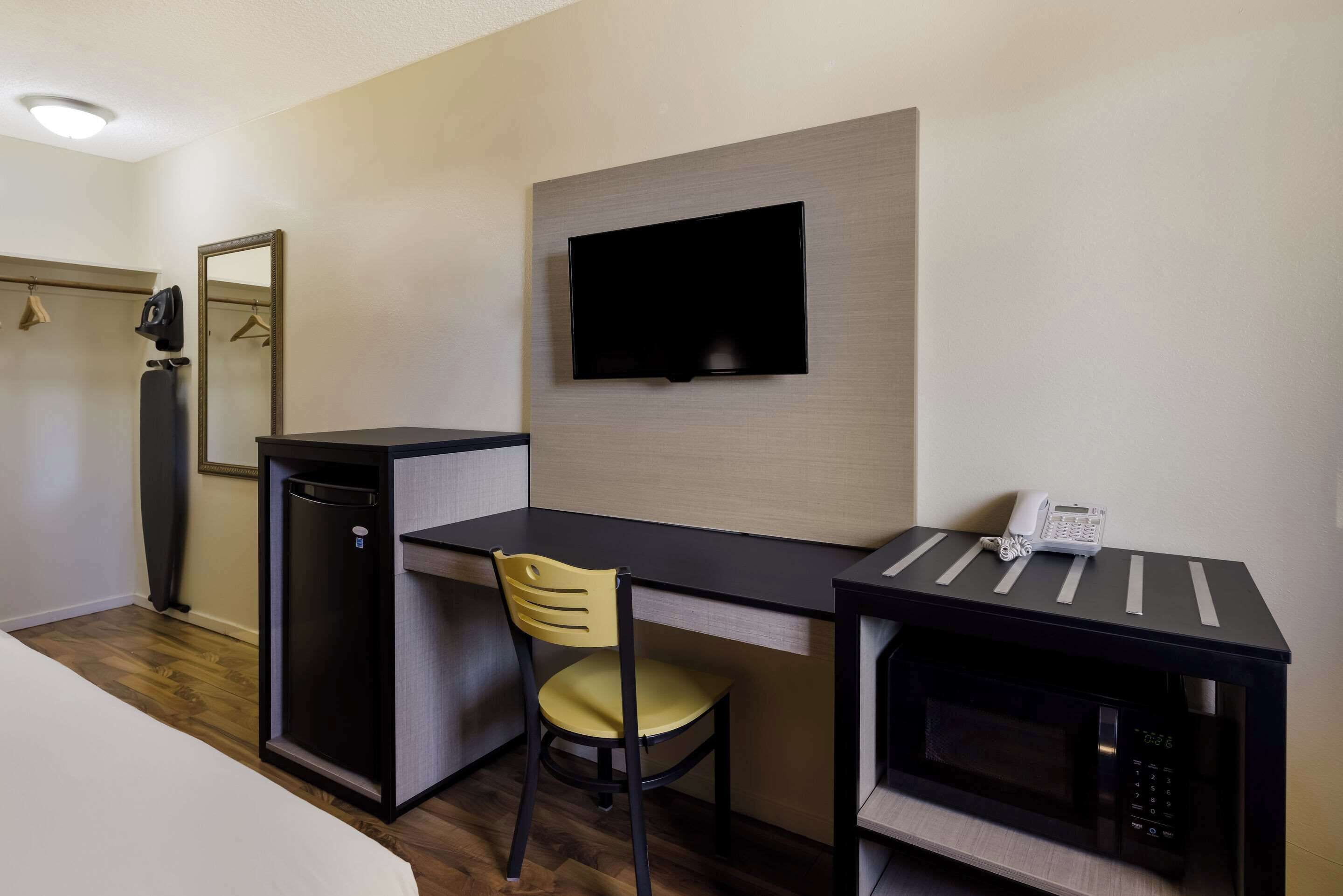 Quarto de hotel compacto com escrivaninha, cadeira, micro-ondas e um pequeno frigorífico.