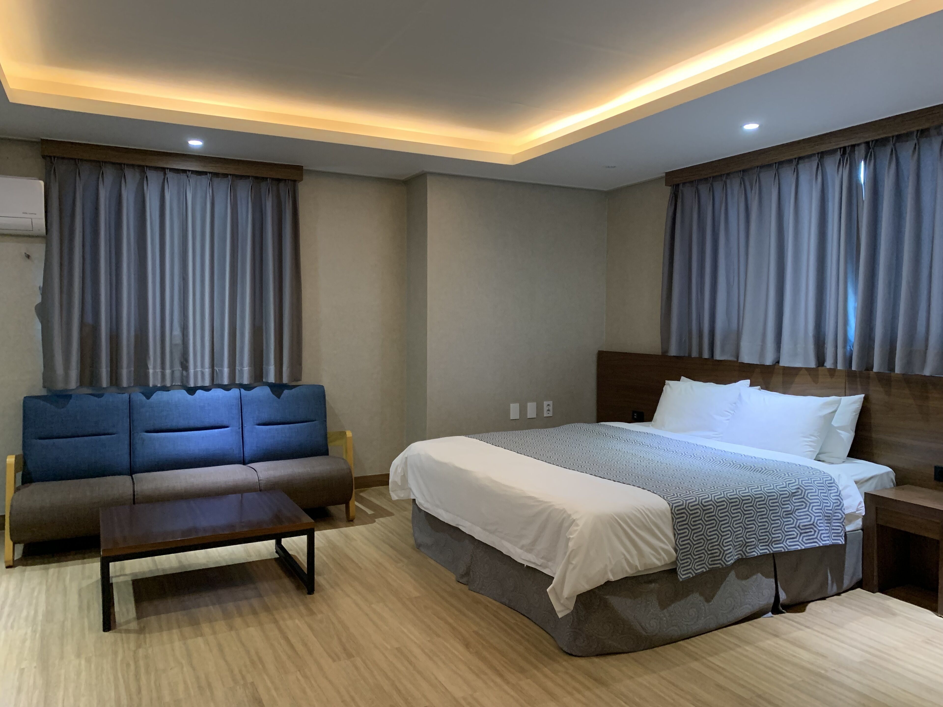Quarto de hotel moderno com uma cama grande, um sofá, uma mesa pequena e um lustre.