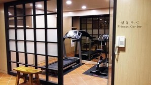 Centro de ginástica com equipamentos de exercício, divisória de madeira e um pequeno banquinho.