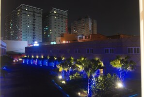 Vista noturna de um edifício com vários andares, janelas iluminadas e um estacionamento com um carro.