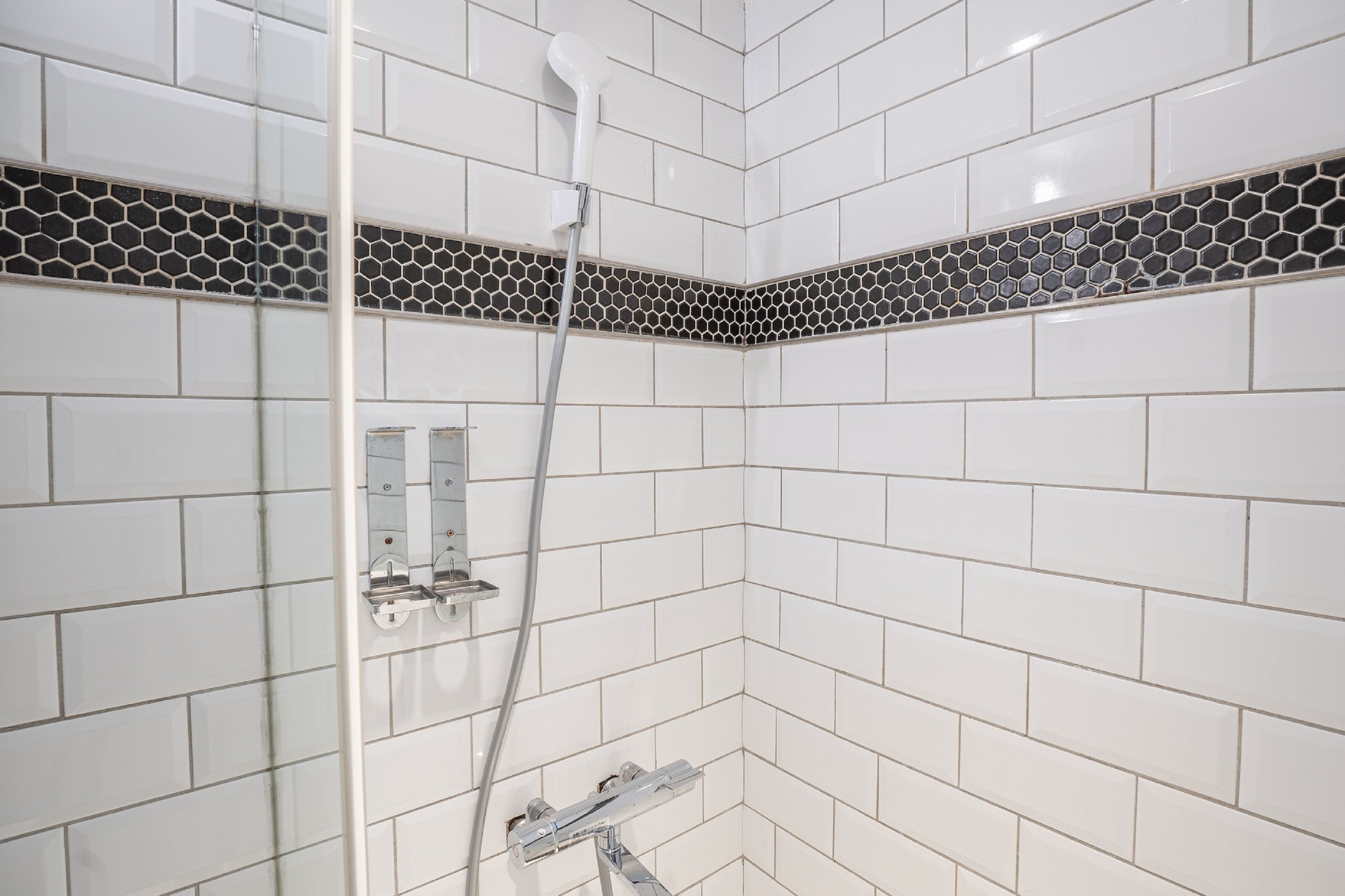 Área de chuveiro com azulejos brancos e borda com padrão hexagonal preto e branco.