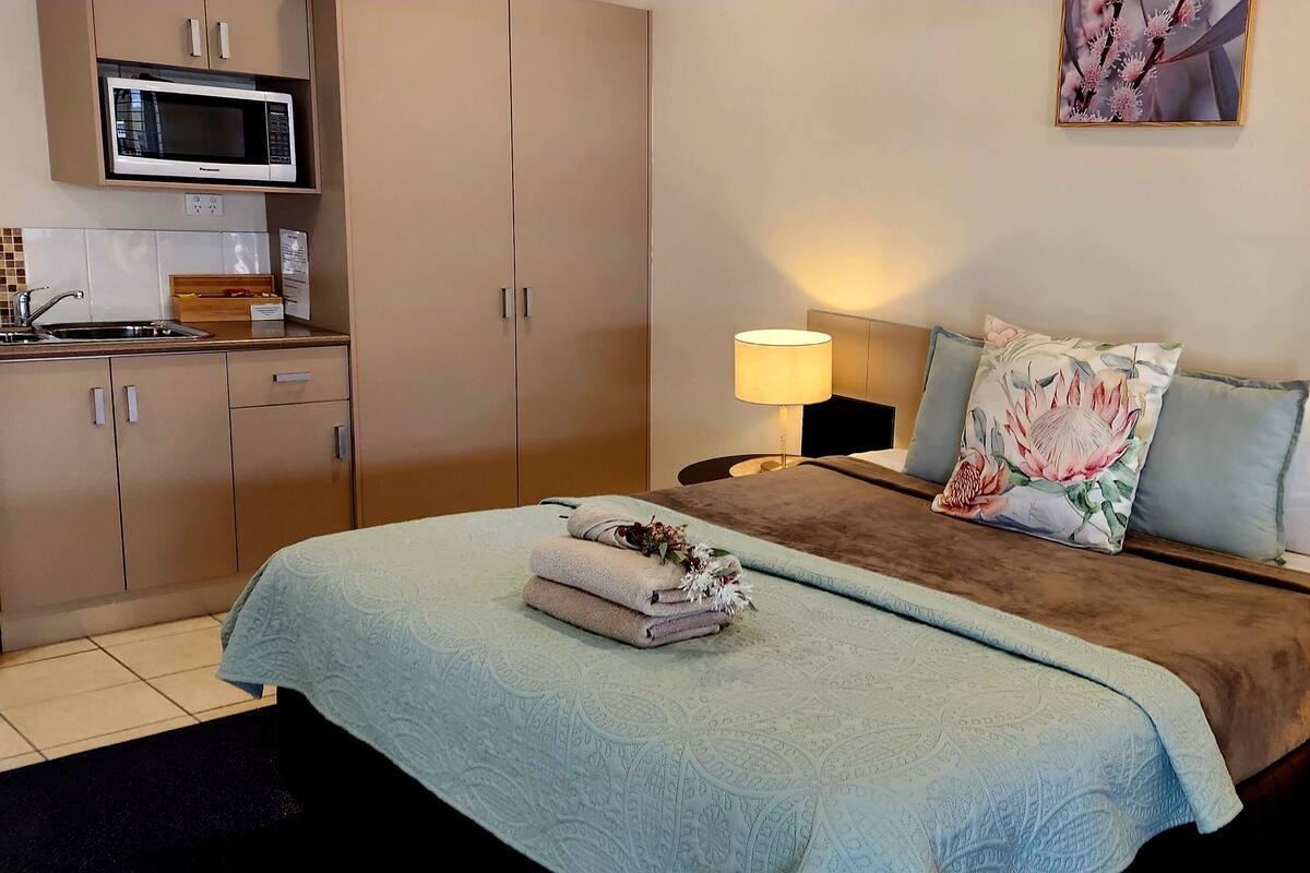 Quarto de hotel com cama, duas luminárias de cabeceira, micro-ondas, pia e armário.