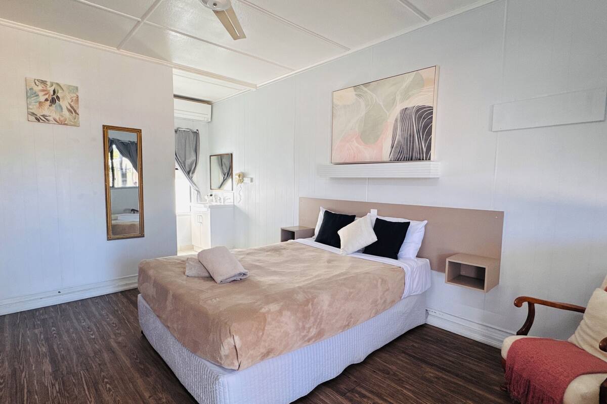 Um quarto com uma cama grande, uma mesinha de cabeceira, uma cadeira e um quadro na parede.