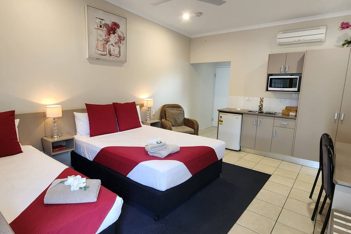 Quarto de hotel com duas camas, cozinha compacta, área de refeições e banheiro.