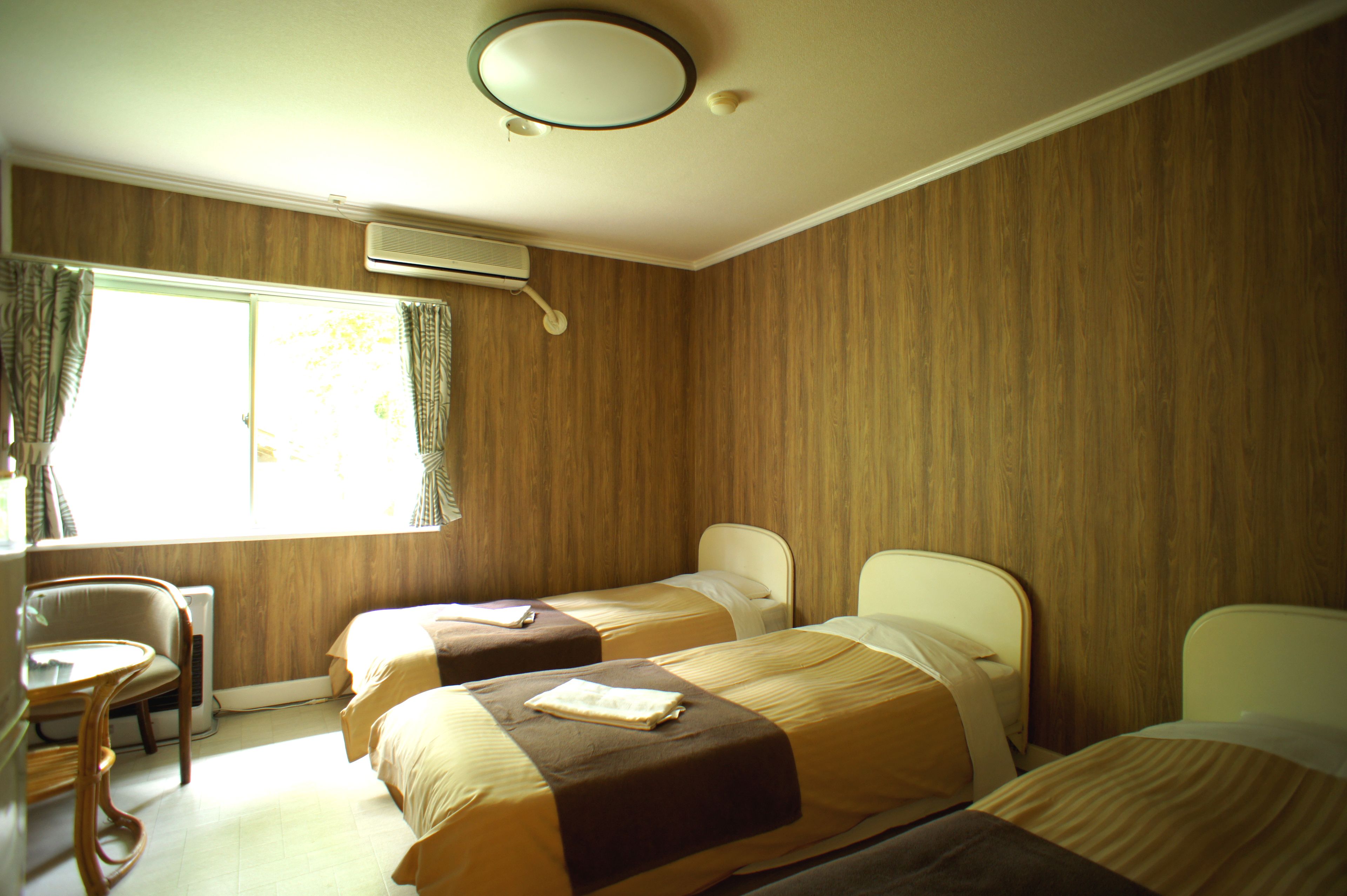 Quarto de hotel com duas camas, uma cadeira, uma mesa e uma janela com cortinas.