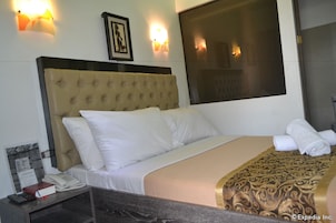 Quarto de hotel com uma cama grande, mesa de cabeceira com telefone e um livro, e luminárias fixadas na parede.