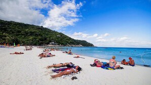 Uma praia com pessoas se banhando ao sol, rodeada por vegetação exuberante e águas azul-claras.