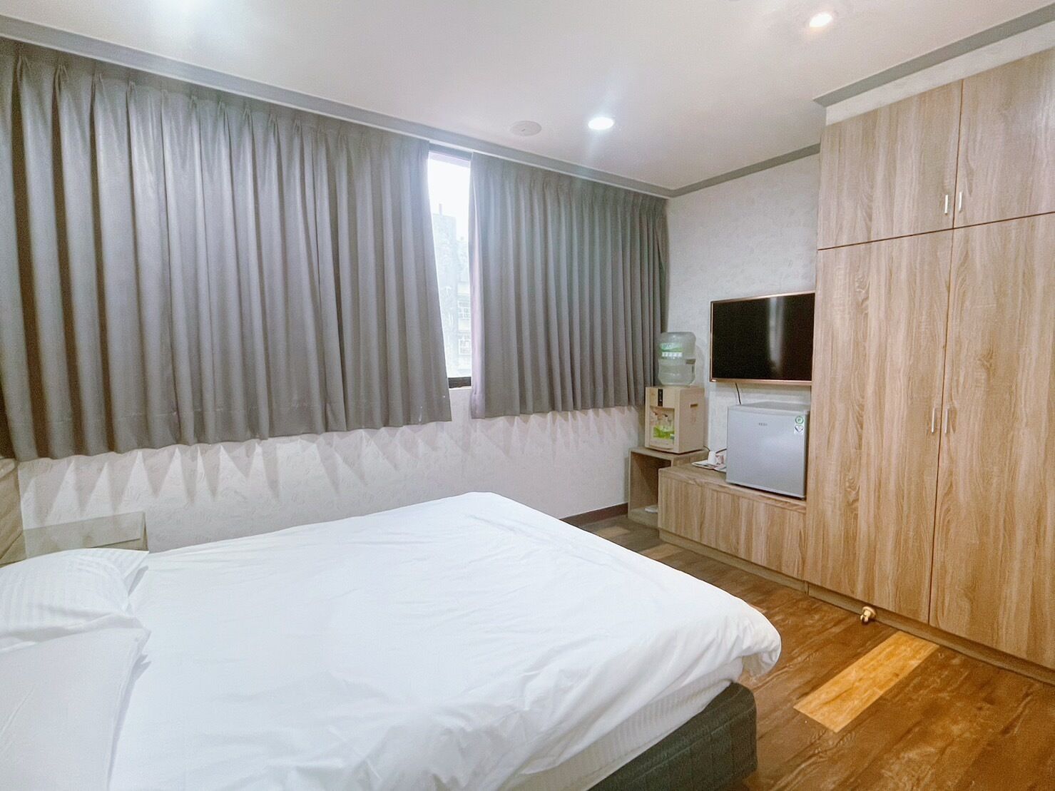 Quarto de hotel com cama, televisão, guarda-roupa e janela com cortinas.