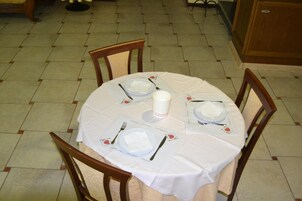 Mesa de jantar redonda com toalha branca, quatro cadeiras e um castiçal no centro.