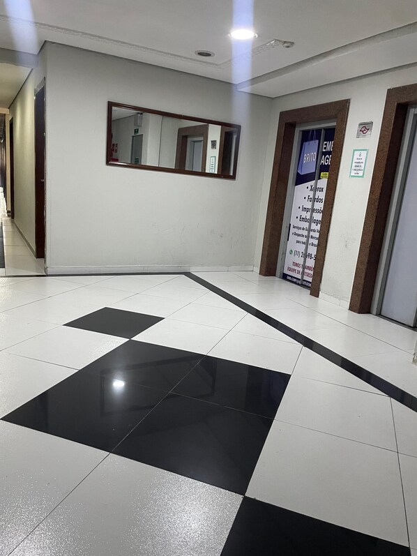 Um saguão de hotel com padrão de piso quadriculado, um espelho na parede e uma porta com uma placa.