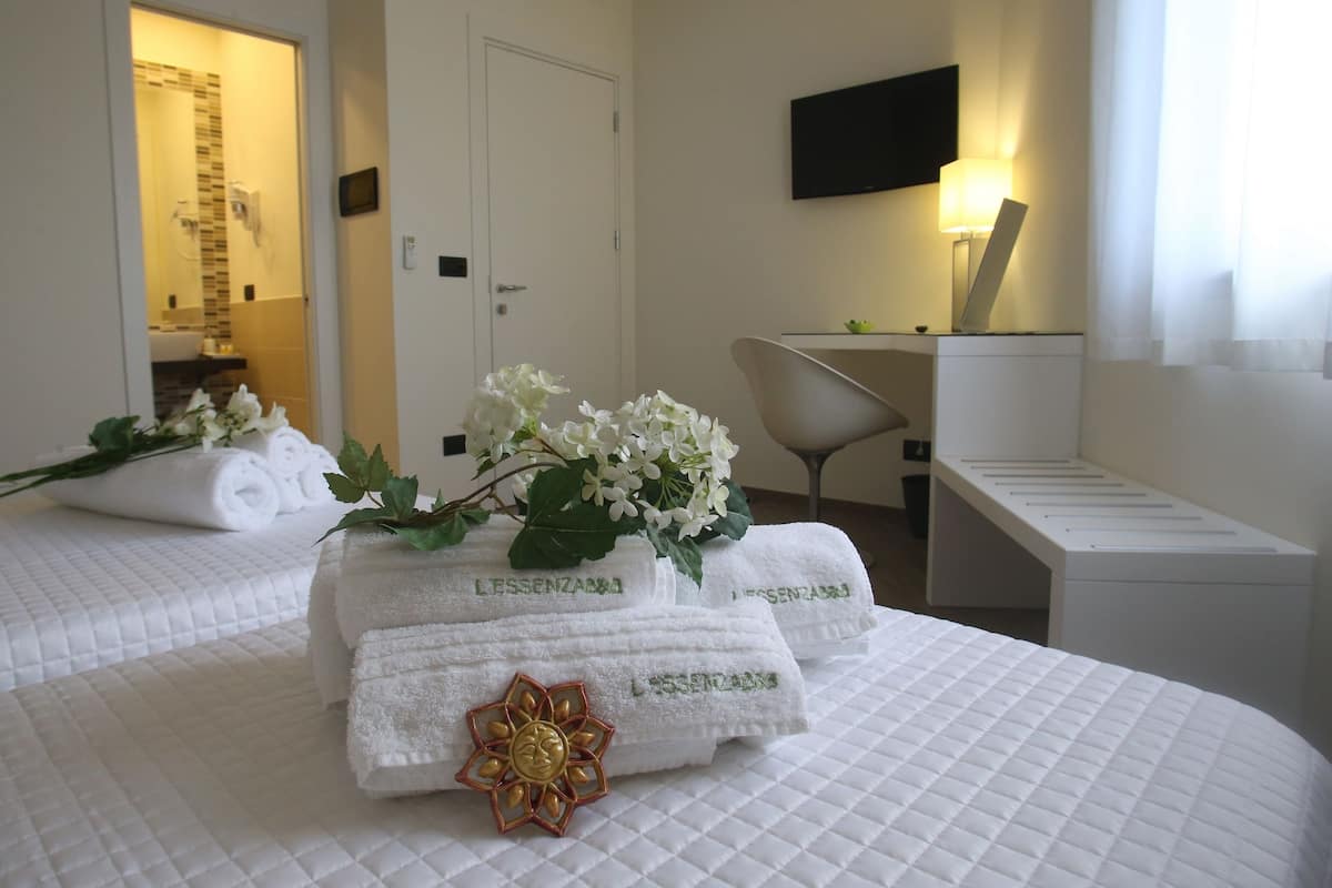 Quarto de hotel com duas camas, uma escrivaninha, uma cadeira, televisão e banheiro visível através de uma porta aberta.
