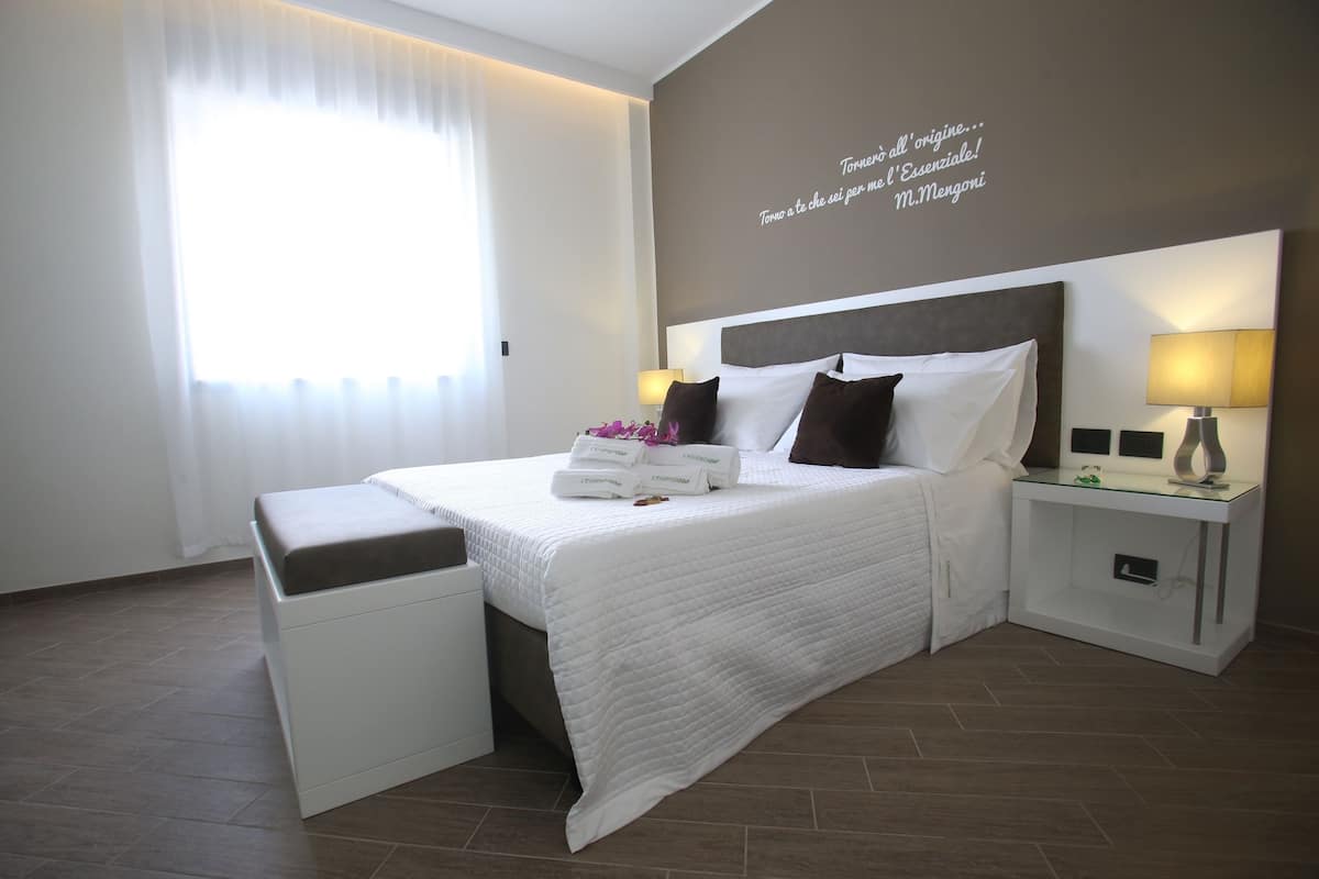 Quarto de hotel moderno com uma cama grande, mesa de cabeceira com abajur e luminária na parede.