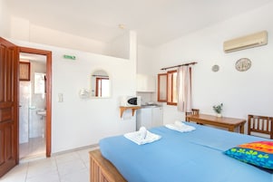 Quarto de hotel com cama, escrivaninha, cadeira, micro-ondas, mesinha e janela com cortinas.