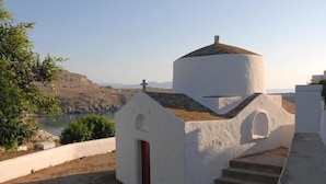 Uma igreja branca com cúpula e torre do sino, rodeada por uma paisagem costeira.