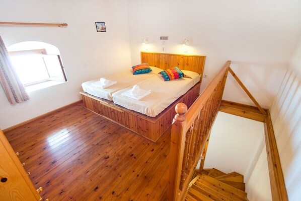 Quarto com cama de madeira, duas almofadas, cabeceira, escada de madeira e uma janela.
