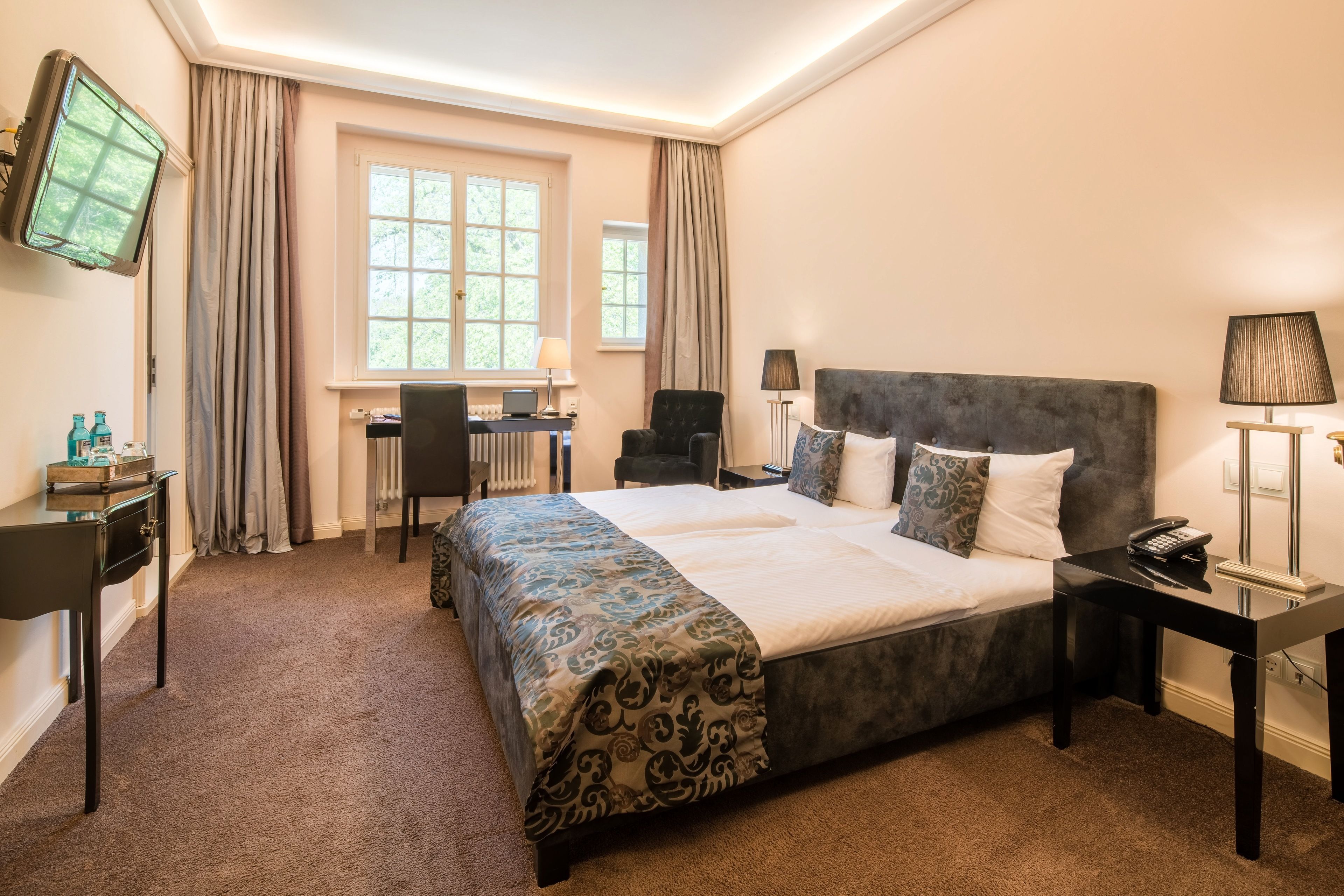 Quarto de hotel com uma cama grande, uma escrivaninha, uma cadeira e uma televisão na parede.