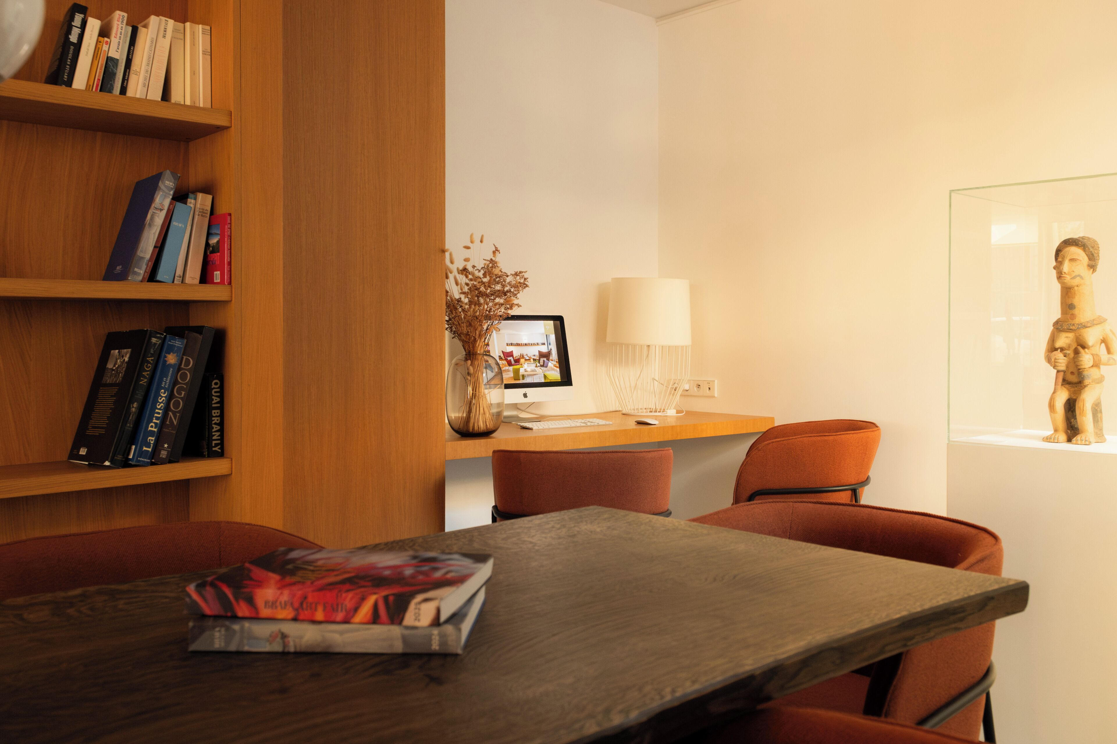 Quarto moderno com estante de madeira, escrivaninha com computador, luminária e uma estátua.