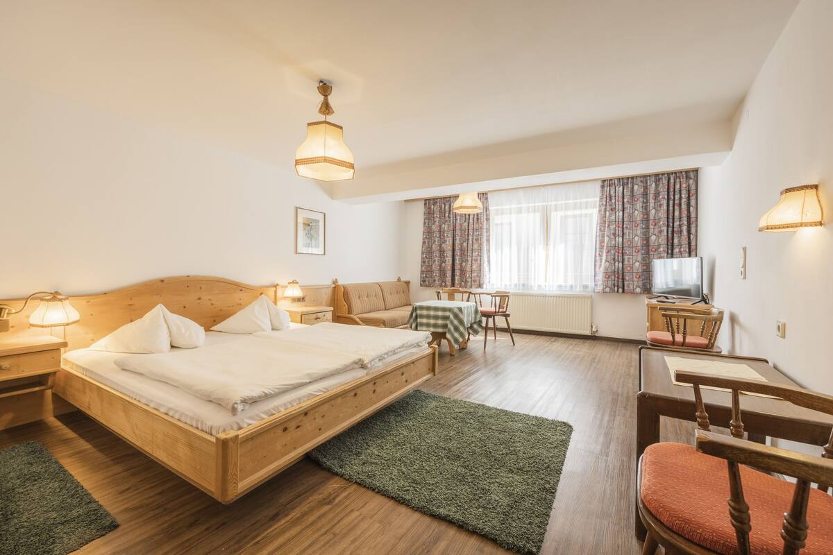Quarto com cama de madeira, escrivaninha, cadeira, sofá e televisão.