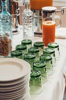 Uma mesa com diversos recipientes de vidro, incluindo um jarro de suco de laranja e algumas garrafas verdes.
