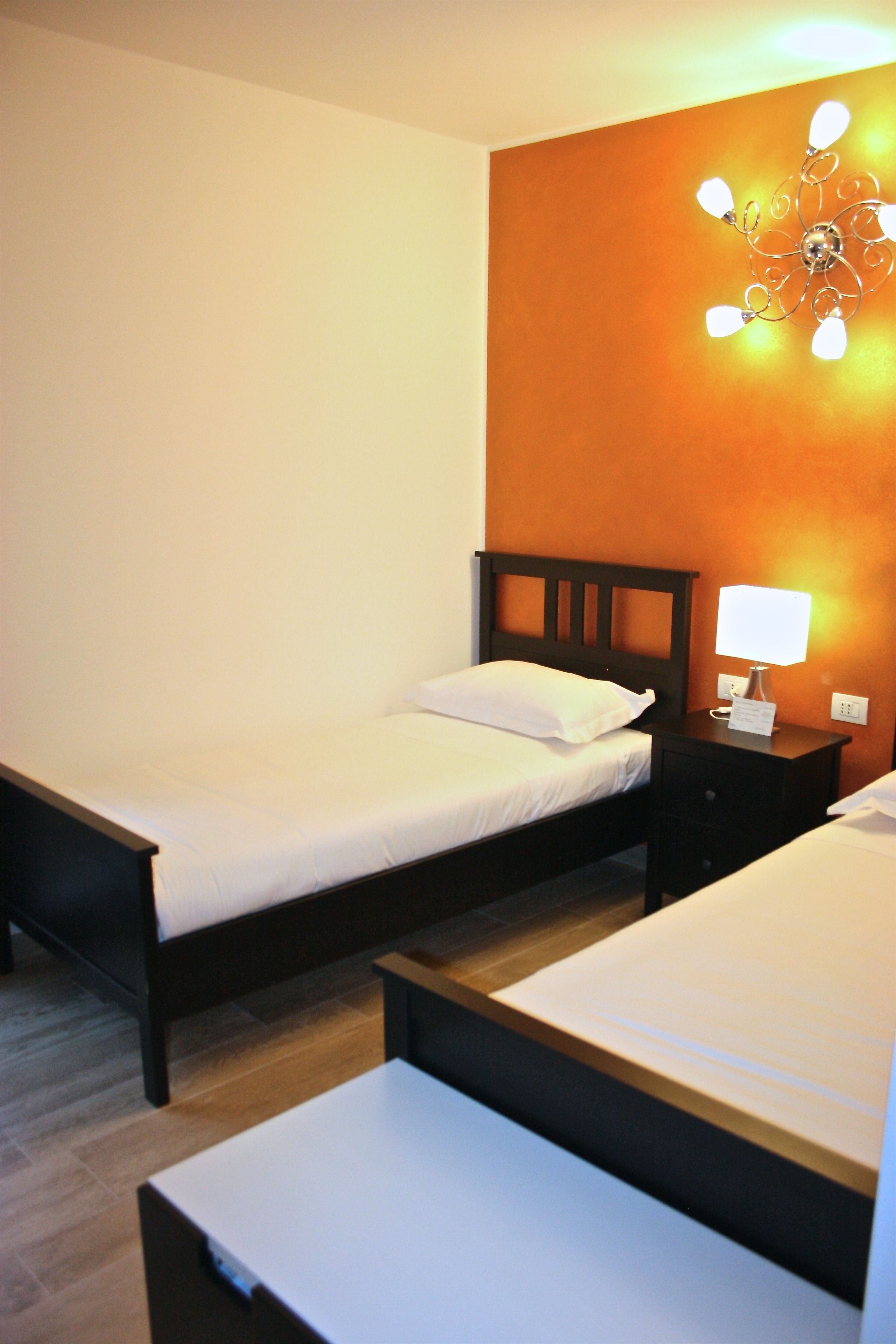 Quarto de hotel com duas camas de solteiro, mesa de cabeceira com luminária e luminária na parede.