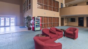 Um hall amplo com poltronas vermelhas, máquina de refrigerantes Coca-Cola e uma grande parede envidraçada.