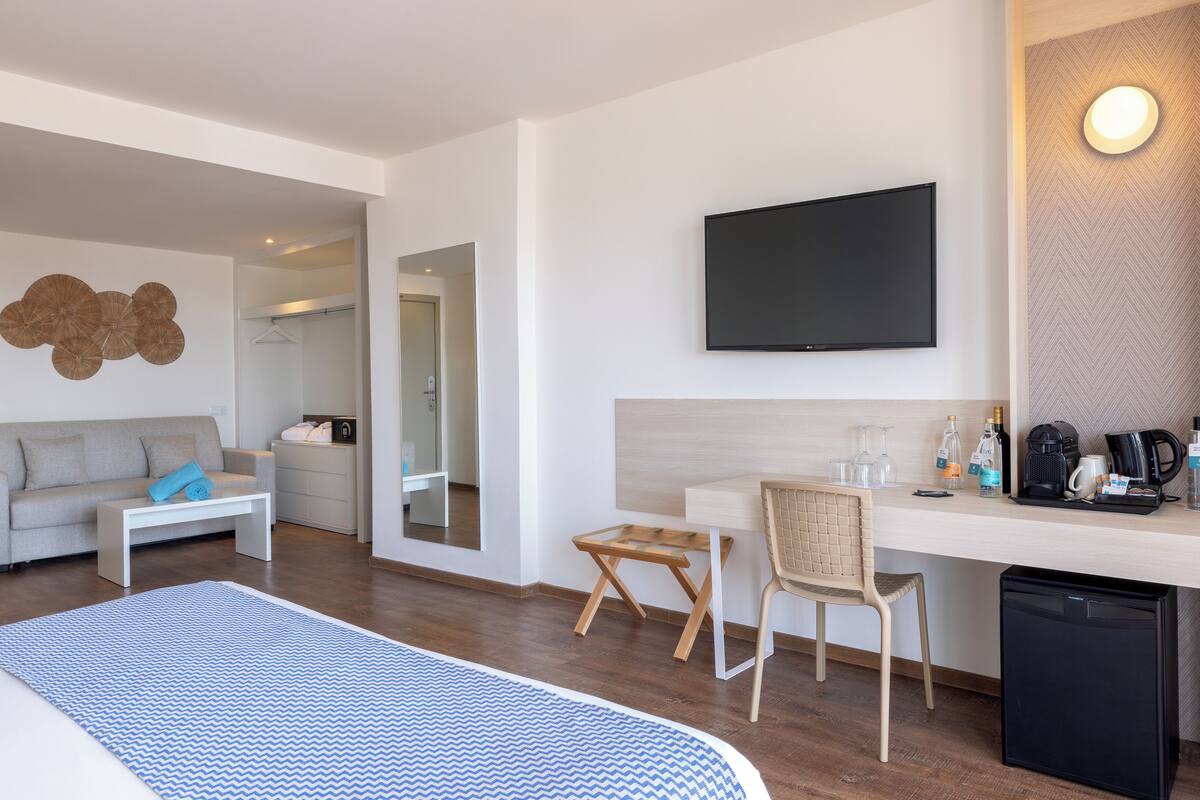 Quarto de hotel moderno com cama, sofá, escrivaninha com cadeira, televisão e máquina de café.