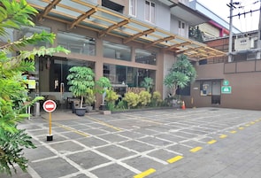 Entrada de hotel com placa de proibido, galeria coberta e plantas em vasos.