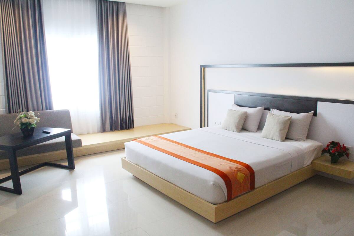 Quarto de hotel com uma cama, mesa de cabeceira e pequena escrivaninha com cadeira.
