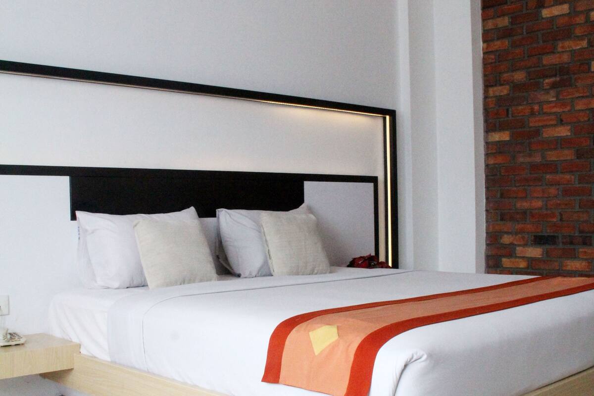 Quarto de hotel moderno com uma cama grande, cabeceira de madeira e parede decorada com tijolos.