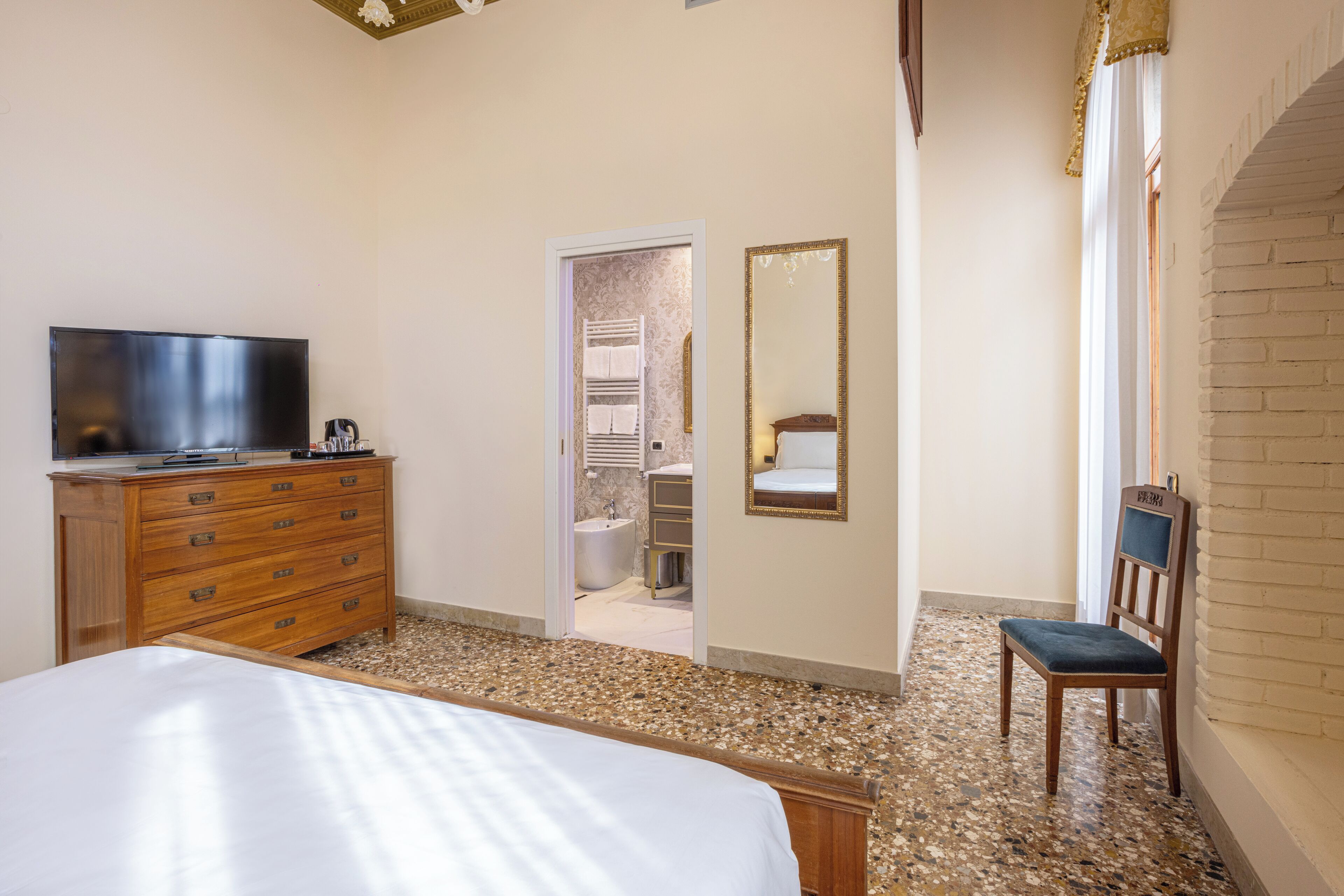Quarto com cama, cômoda de madeira, televisão, espelho e cadeira.