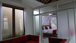 Quarto com sofá vermelho, cama com dossel e porta de vidro deslizante que dá para uma varanda.
