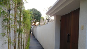 Um caminho estreito ladeado por bambus, conduzindo a uma porta de madeira.