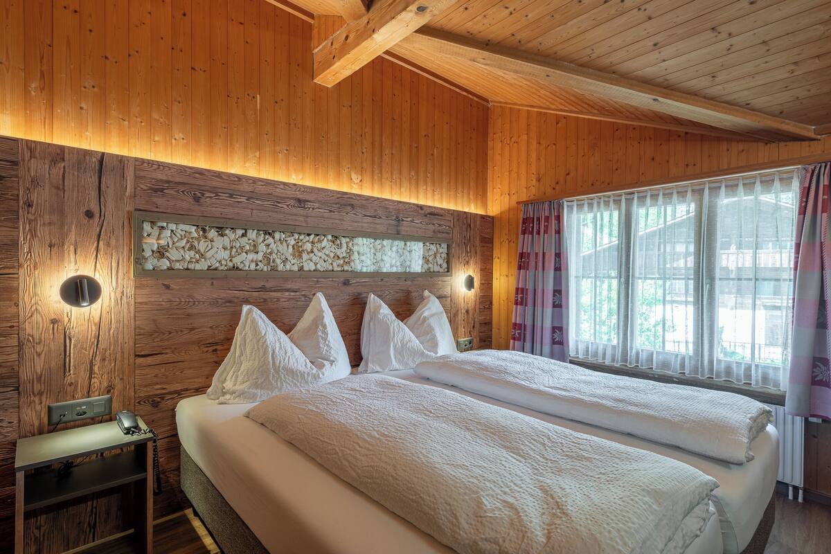 Quarto com painéis de madeira, uma cama grande, abajures e uma janela com cortinas.