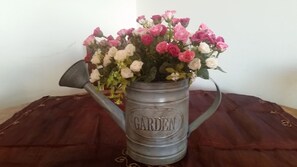 Um regador de metal com a palavra 'GARDEN' gravada, cheio de flores rosa e brancas.