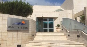 Entrada de um edifício com uma placa indicando 'marina village' e uma escadaria que leva até ele.