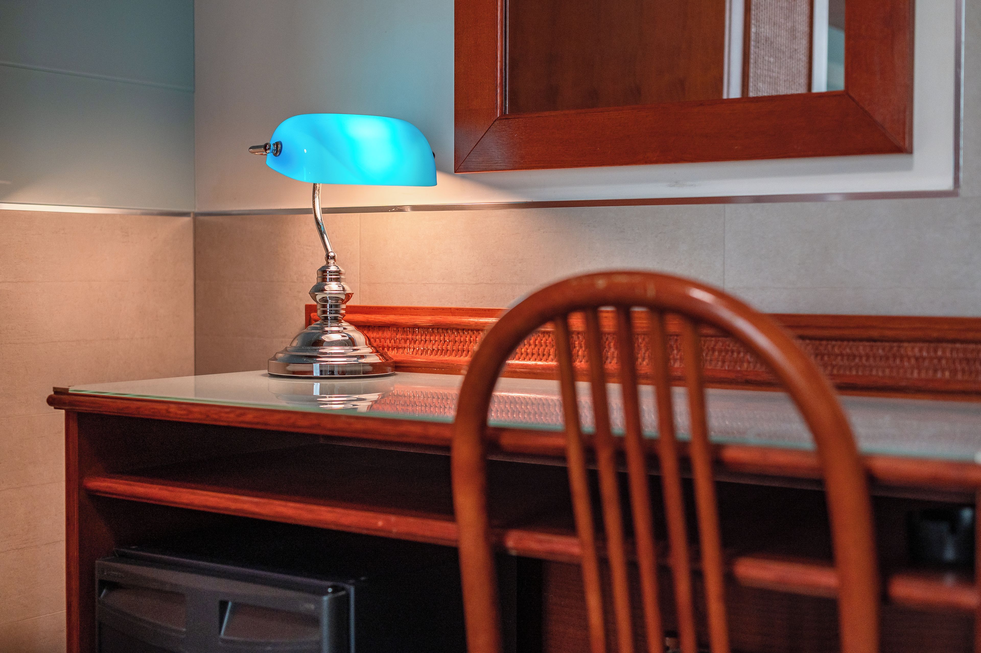 Uma mesa de madeira com uma luminária, uma cadeira e um armário ao fundo.