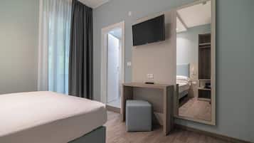 Quarto de hotel com cama, escrivaninha, cadeira, televisão e guarda-roupa.