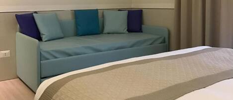 Quarto de hotel com cama, sofá com almofadas, janela com cortinas e parede listrada.