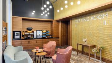 Uma sala de reuniões moderna com cozinha, armários de madeira e disposição de assentos incluindo duas cadeiras e uma mesa.