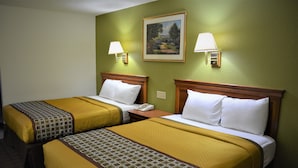 Quarto de hotel com duas camas, cada uma com cabeceira de madeira, roupa de cama branca e colcha estampada. Há luminárias na parede e um quadro sobre as camas.