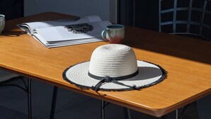 Uma mesa de madeira com um chapéu branco, um livro e uma caneca.