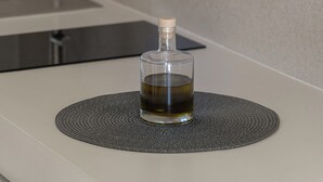 Uma cozinha com bancada, uma garrafa de azeite e um tapete texturizado.