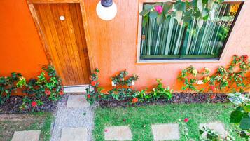 Uma casa com porta de madeira, janela com vista para bambus e um jardim com pedras no chão e flores.