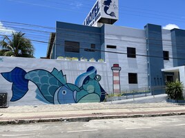 Um edifício com um mural de um peixe e um farol, apresentando uma placa com a inscrição 'Hotel do Sereia'.