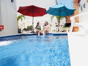 Piscina com duas pessoas sentadas sob guarda-sóis.