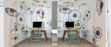 Quarto com parede espelhada com motivos florais, uma coluna central e duas mesas de escritório com cadeiras.