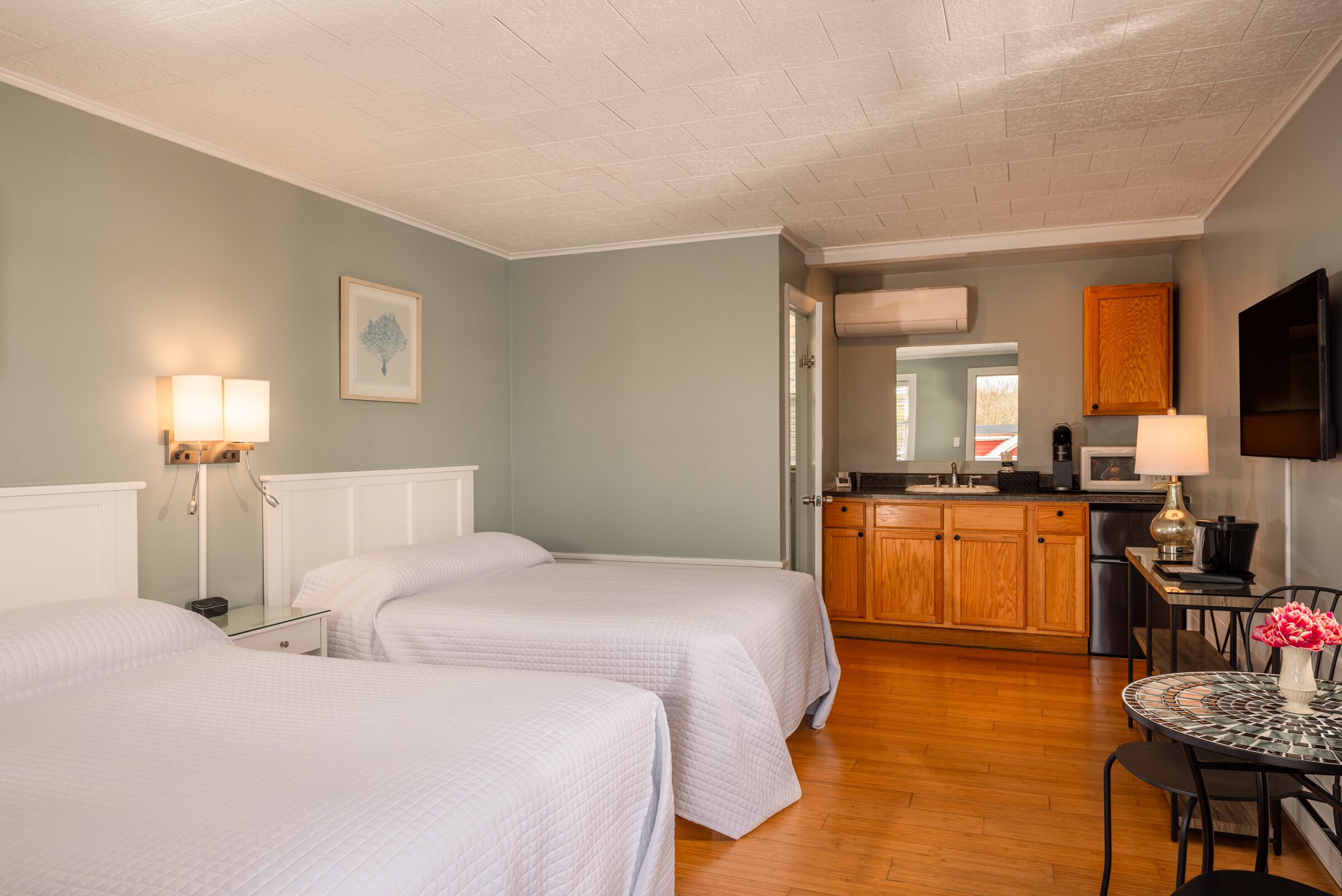 Quarto de hotel com duas camas, cozinha compacta, área de refeições e televisão.