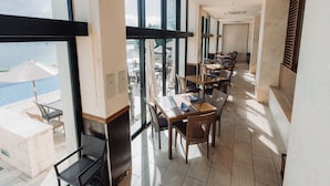 Restaurante moderno com grandes janelas, mesas ao ar livre e vista para o mar.