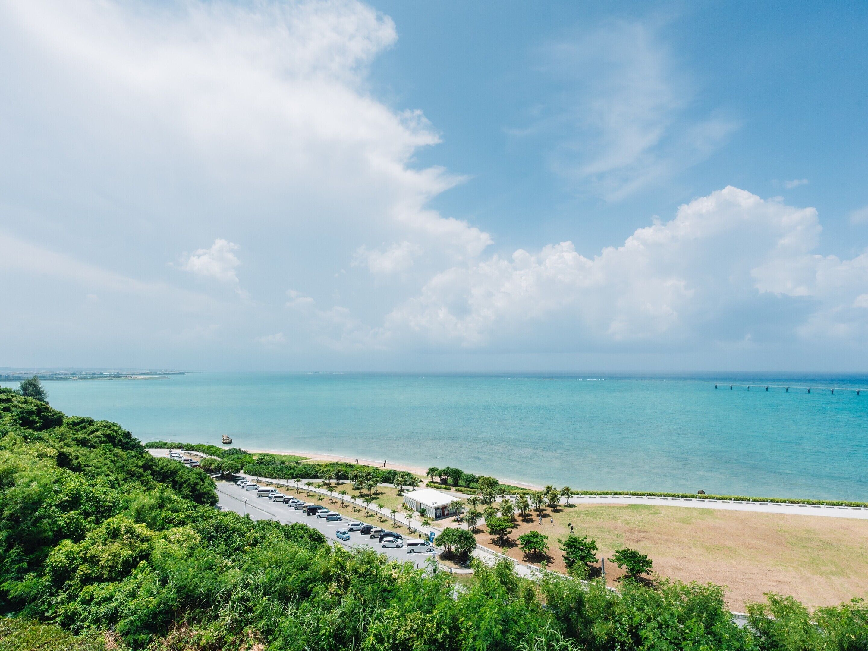 Vista costeira com parque de estacionamento, praia e vegetação.